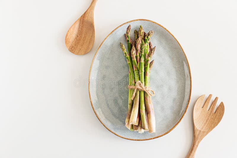 Fresh Asparagus Tied Bundle on Plate and Wooden Utensils on White Table ...