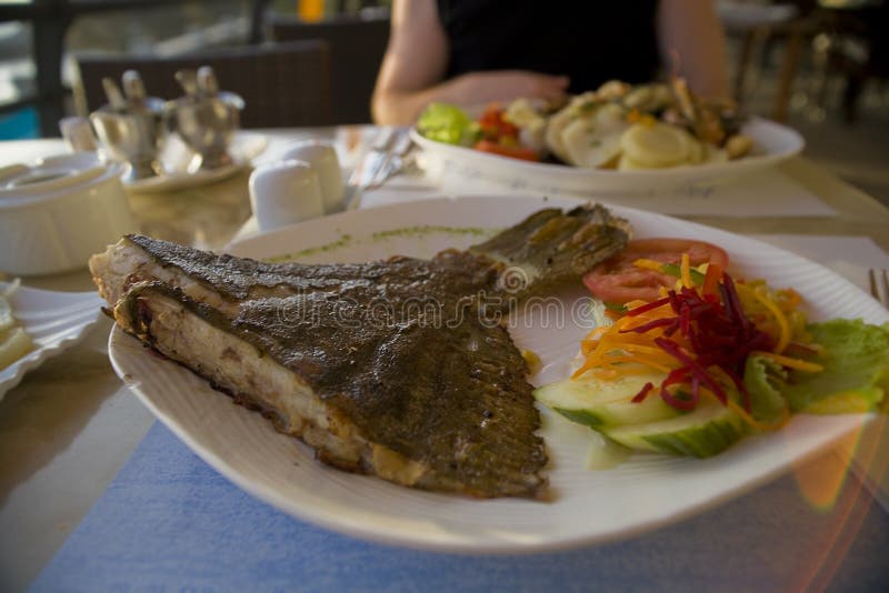 Fried Half of a Large Fish Served on a White Plate with Vegetables in a ...