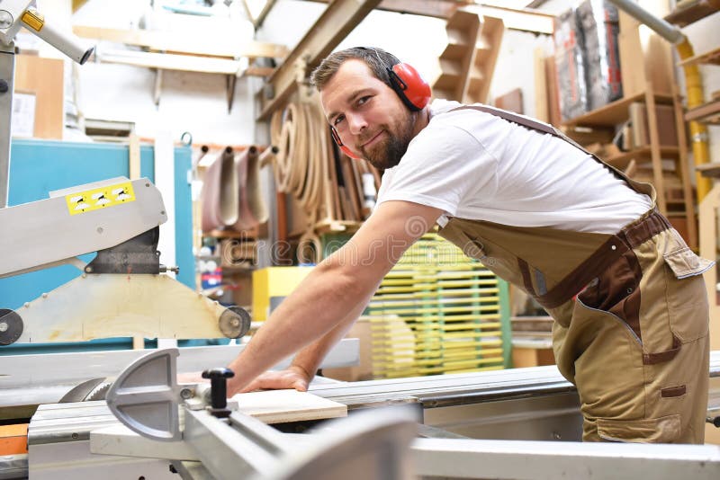 Friendly Carpenter with Ear Protectors and Working Clothes Working on a ...