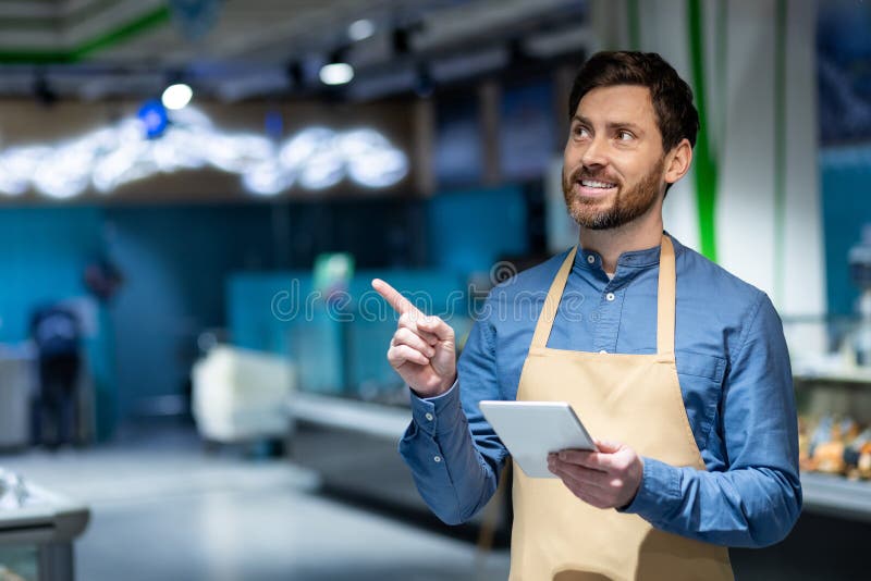 Friendly Shopkeeper Using Tablet in Grocery Store while Pointing and ...
