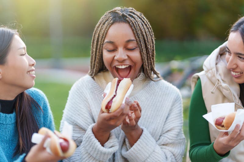 Friends Eating Hot Dogs in a Park Stock Photo - Image of discussing ...