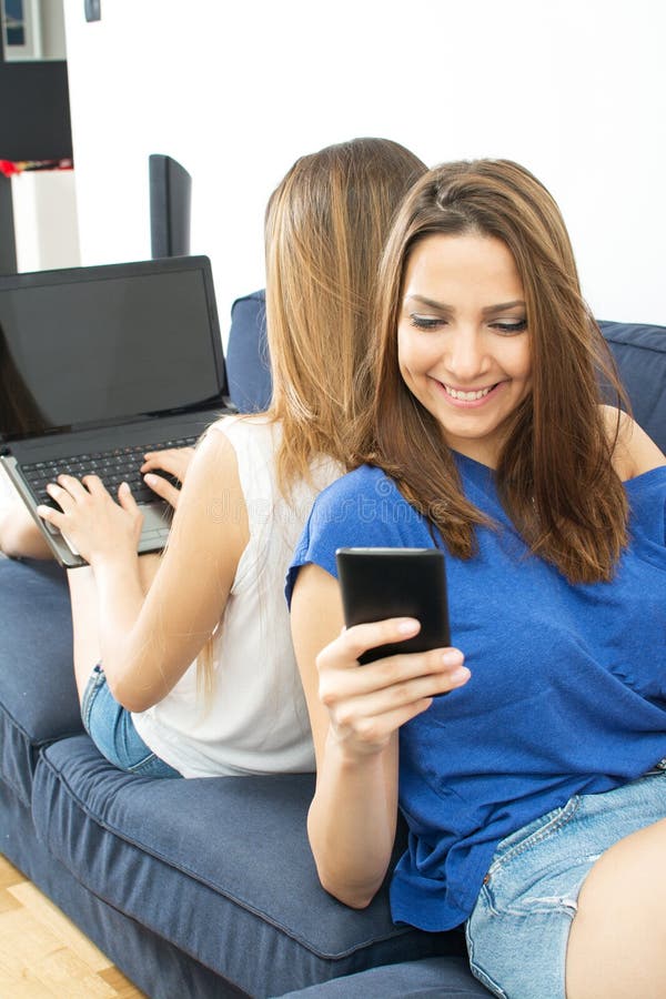 Friends Sitting Back To Back and Using Phone and Laptop at Home. Stock ...