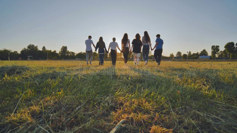 Friends at Sunset Holding Hands Walking Towards the Sun. Stock Image ...