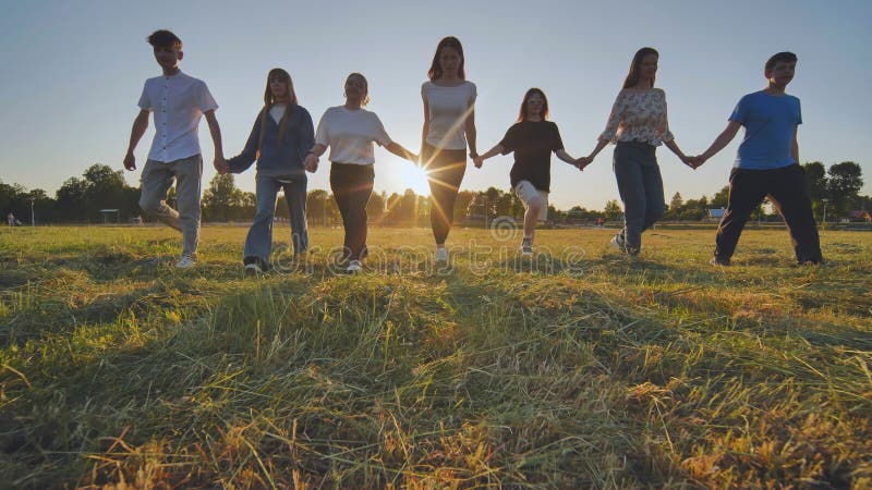 Friends at Sunset Holding Hands Walking Towards the Sun. Stock Image ...