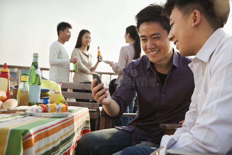 Friends Using Cell Phone at Rooftop Barbecue Stock Photo - Image of ...