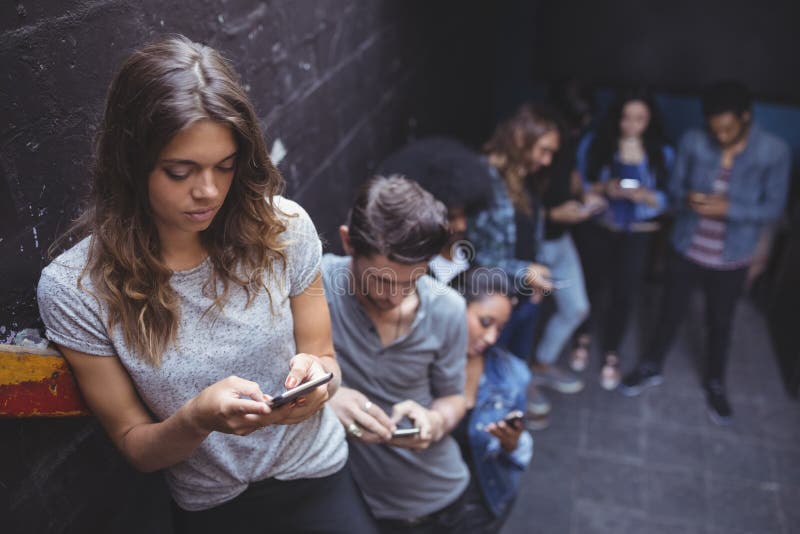 Friends Using Mobile Phones while Standing by Wall Stock Image - Image ...