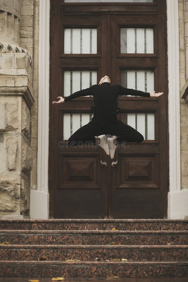 Front Image of a Dancer Dressed in Black Jumping Up Behind a Building ...