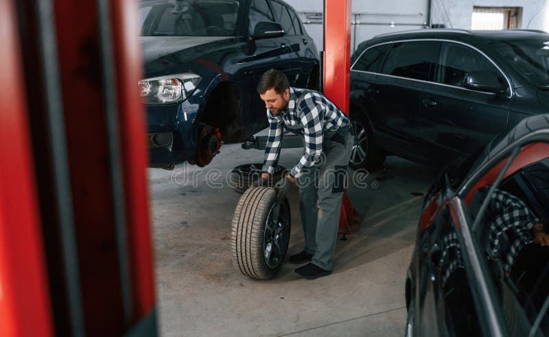 Front Left Wheel is Changing. Man in Uniform is Working in the Auto ...