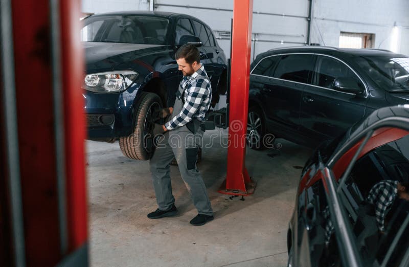 Front Left Wheel is Changing. Man in Uniform is Working in the Auto ...