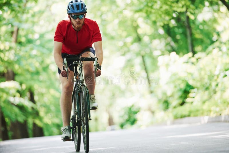 Front View. Cyclist on a Bike is on the Asphalt Road in the Forest at ...