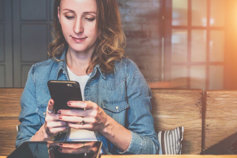 Front View Of Young Woman Sitting In Cafe At Table And Use Smartphoneon Table Is Tablet