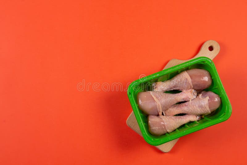 Frozen Chicken Legs in a Plastic Container on Orange Background Stock ...