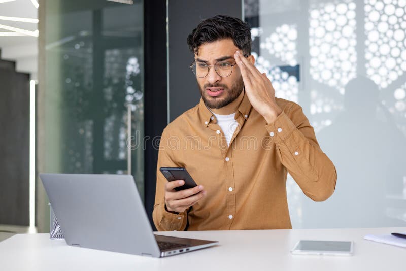 Frustrated Man Using Phone and Laptop in Office, Solving Problem ...