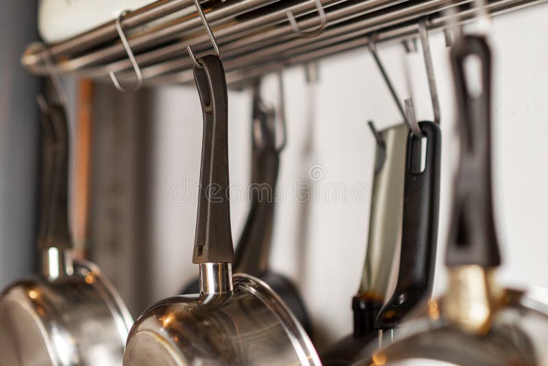Frying Pans and Kitchen Utensils Hang on Hooks in the Kitchen. Storage ...