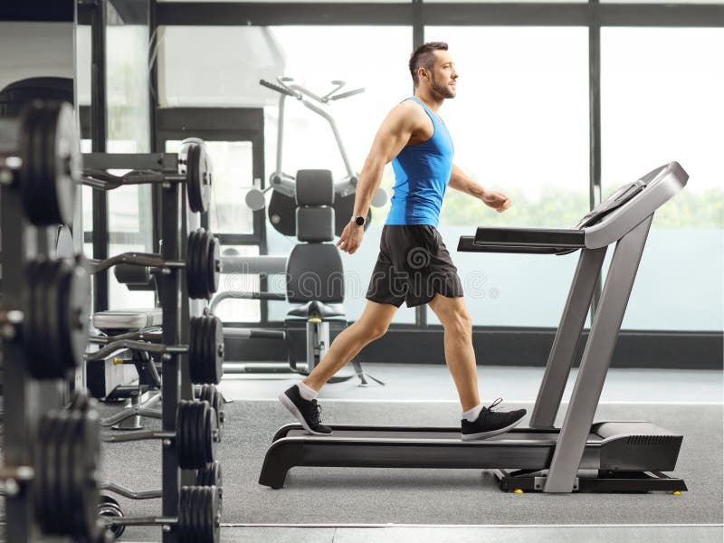 Full Length Profile Shot of a Young Man Walking on a Treadmill in a Gym ...