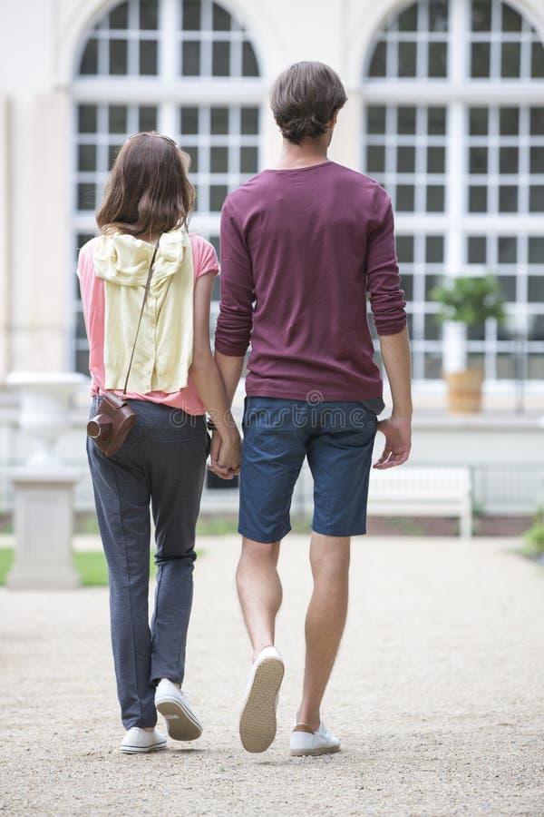 Full-length Rear View of Young Couple Walking Against Building Stock ...
