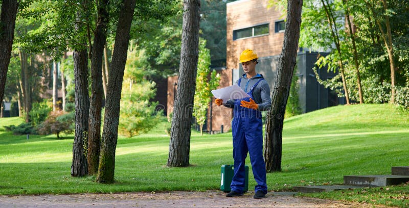 Full Length of Young Builder Standing Outdoors with Blueprint while ...