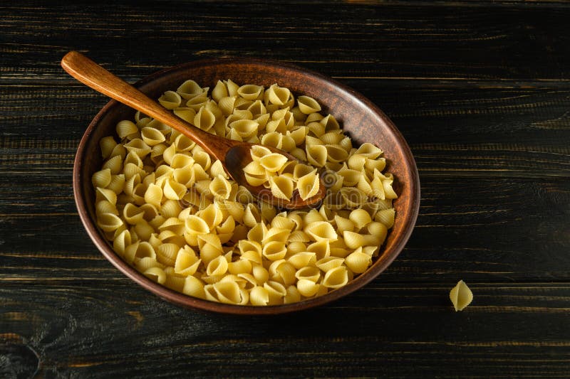 A Full Plate of Shell-type Pasta and a Spoon on an Antique Dark Table ...