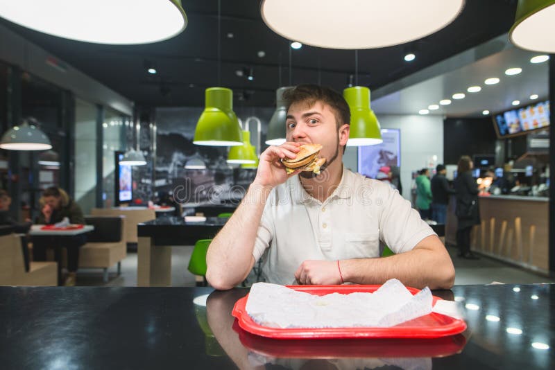 A Funny Man Eats an Appetizing Burger in a Restaurant and Looks at the ...