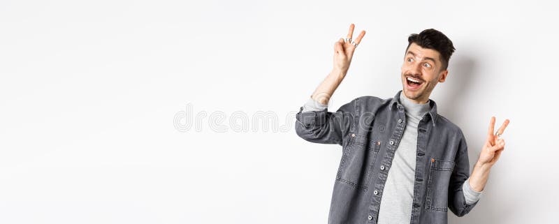 Funny Young Man Showing V-signs and Smiling at Left Side, Looking at ...