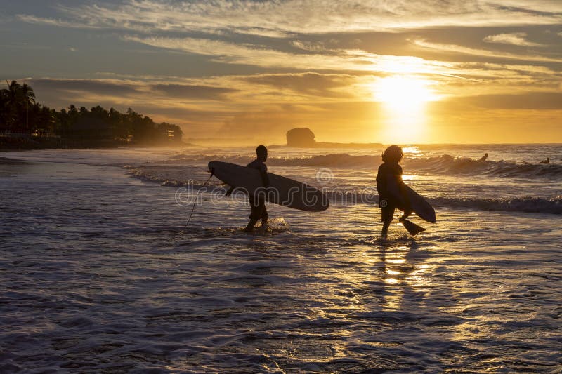 Two Surfers at Sunrise Walking into the Waves on a Tropical Beach Stock ...