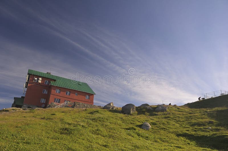 A Vibrant Red Mountain Lodge with a Green Roof Stands on a Grassy Hill ...