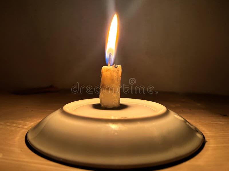A Small Wax Candle with a Bright Flame Sits on a White Ceramic Plate ...