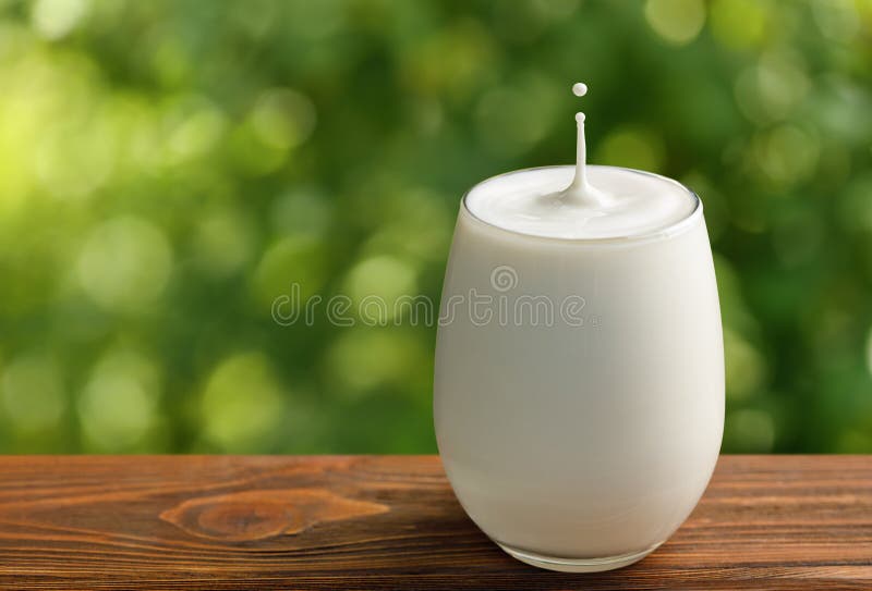 Glass of Milk with Splash and Drop on Table with Green Garden on the ...