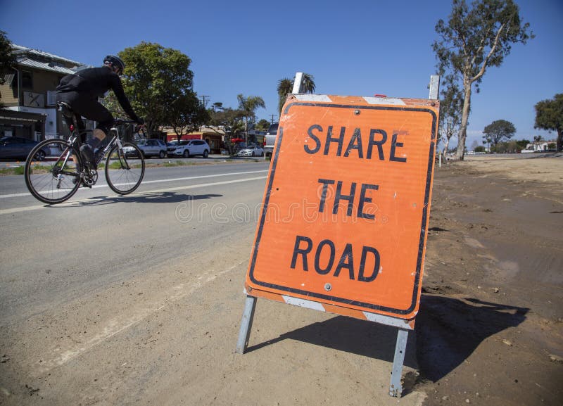 A Road Sign Stating Share the Road with a Bike Passing by on a Street ...