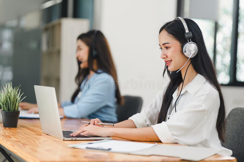 Smiling Call Center Agents Wearing Headsets, Working at Desks with Computers and Documents in a ...