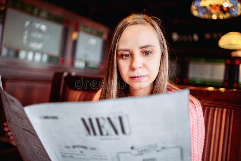 A Woman is Seated at a Table, Attentively Reading a Menu. Stock Photo ...