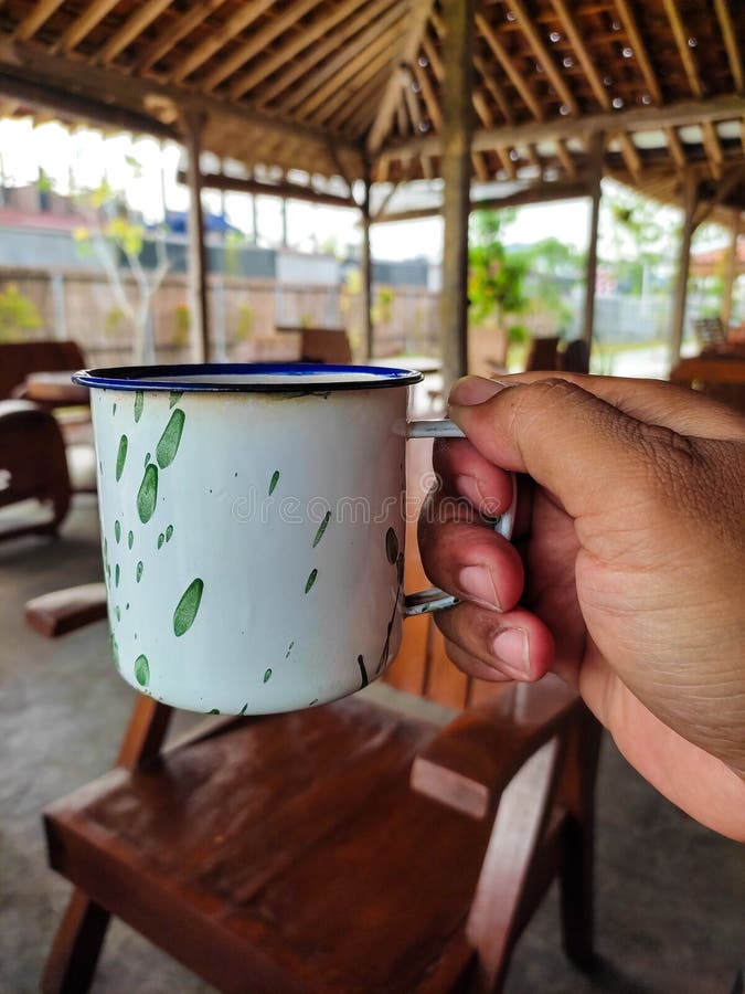 Old Fashioned Enamel Cup in White with Green Prints Held in Hand Stock ...