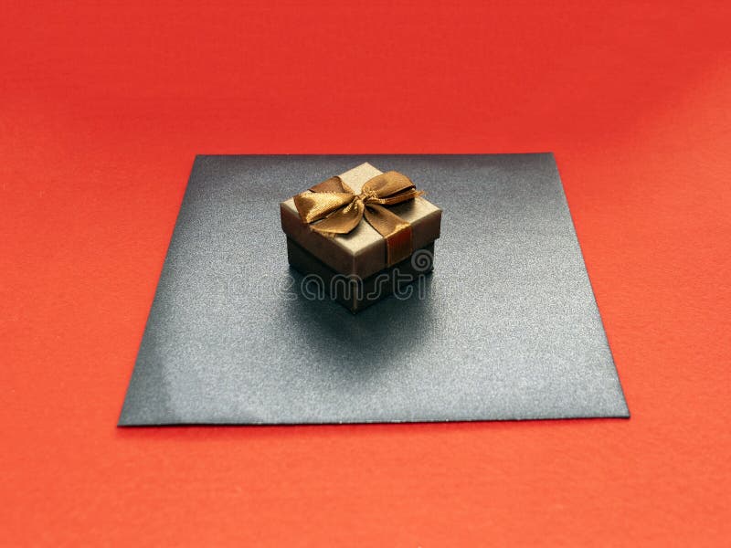 Gift Box in Bronze Color with a Bow and a Black Craft Envelope on a Red ...