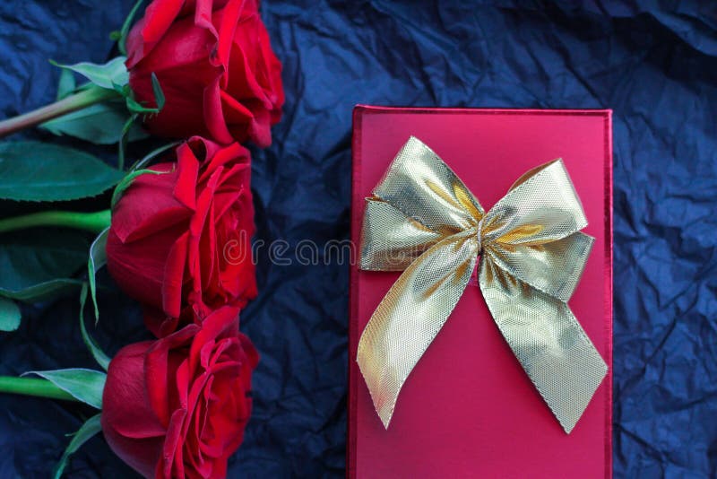 Gift in a Red Box with a Gold Bow and Three Red Roses on a Dark ...