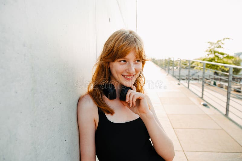 Ginger Woman in Headphones Smiling while Leaning on Wall after Workout ...