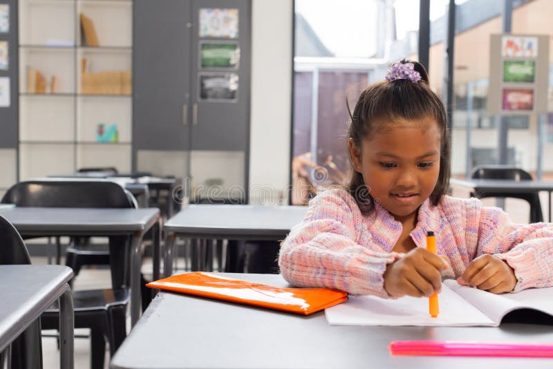 Girl Child Writing in Notebook in Elementary Classroom, Using Orange ...