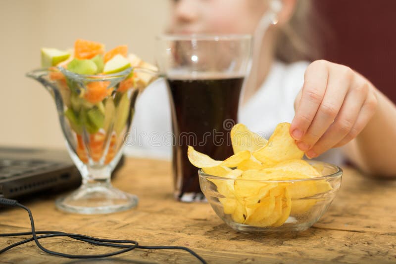Girl Eats Potato Chips and Fruit Salad in Front of Laptop. Stock Image ...