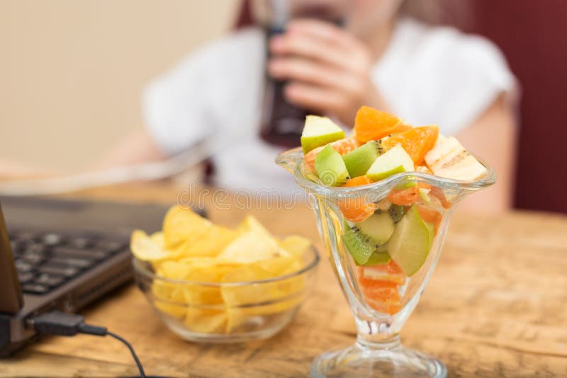 Girl Eats Potato Chips and Fruit Salad in Front of Laptop. Stock Photo ...