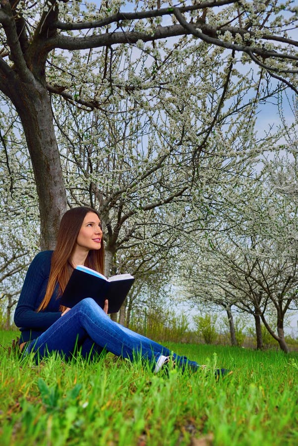 The Girl in the Flowered Garden Sit on the Grass and Reading a B Stock ...