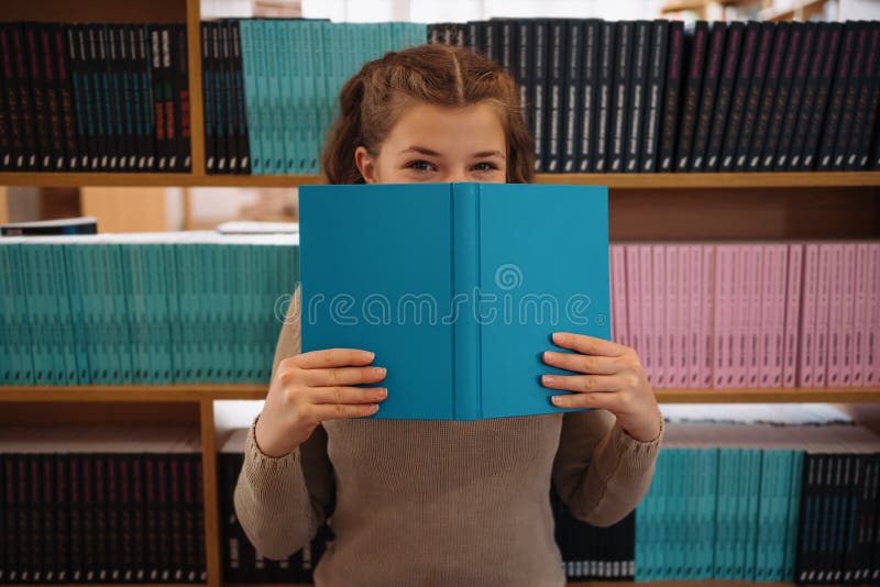 Girl Hiding Face Behind a Book with Bookshelf in Background Stock Image ...