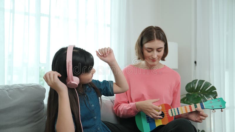 Girl Listening To Music By Using Headphone While Mom Playing Ukulele