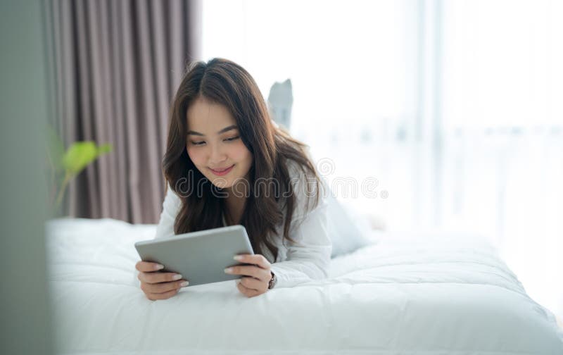 Girl Lying in Bed Playing Tablet Computer in Bedroom with a Smiling ...