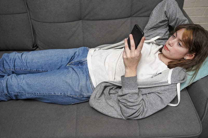 Girl is Lying on the Couch and Holding a Smartphone in Her Hands Stock ...
