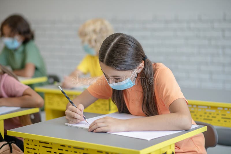 Girl in Mask Writing in a Notebook and Looking Involved Stock Image ...