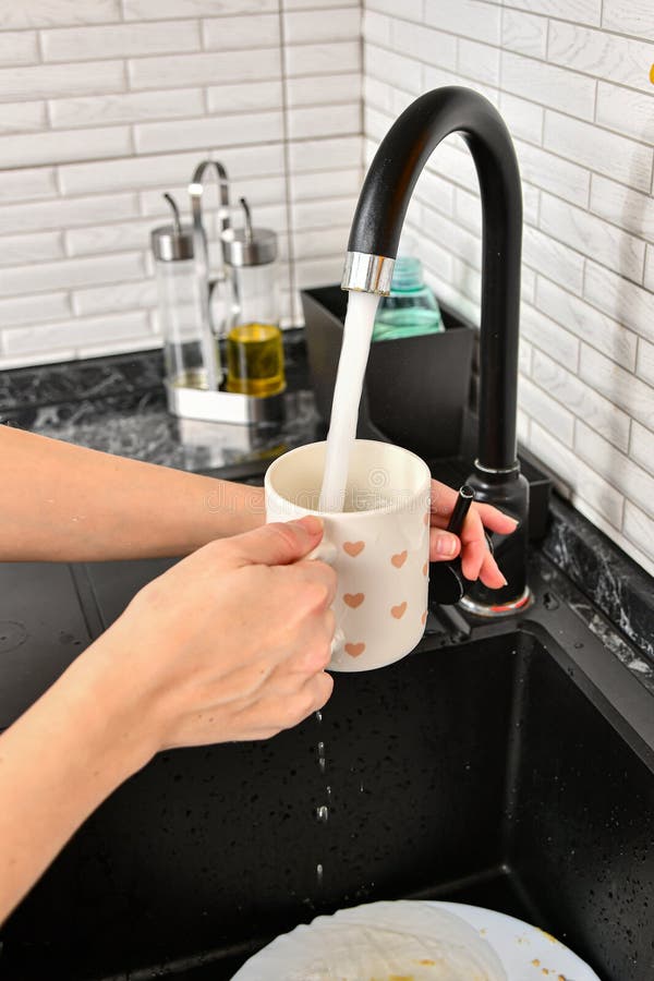 The Girl Pours Water from the Tap in the Kitchen into a Drinking Cup ...