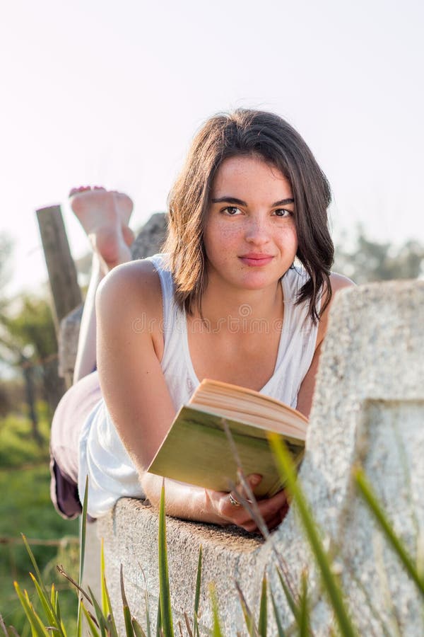 Girl Reading Book Outdoors Looking Up Smiling Stock Photo - Image of ...