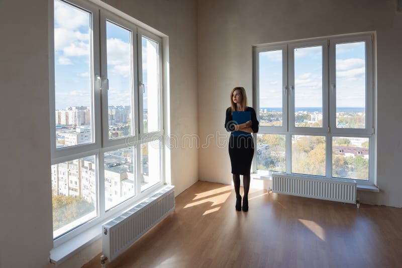 Girl Realtor with a Folder Stands at the Big Windows of a Spacious ...