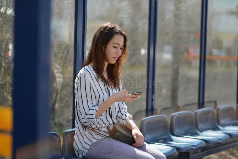 A Girl Sits Alone at a Bus Stop Using a Mobile Phone Stock Image ...