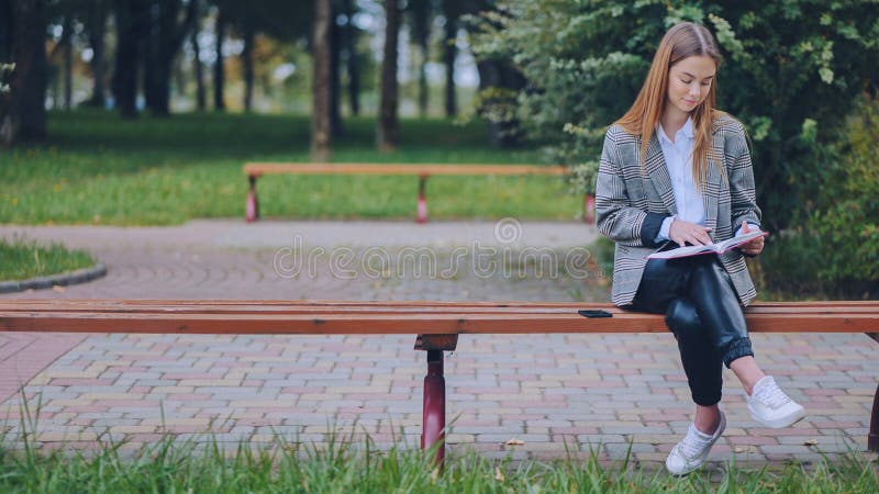 A Girl Sits on a Park Bench and Reads a Book. Stock Photo - Image of ...