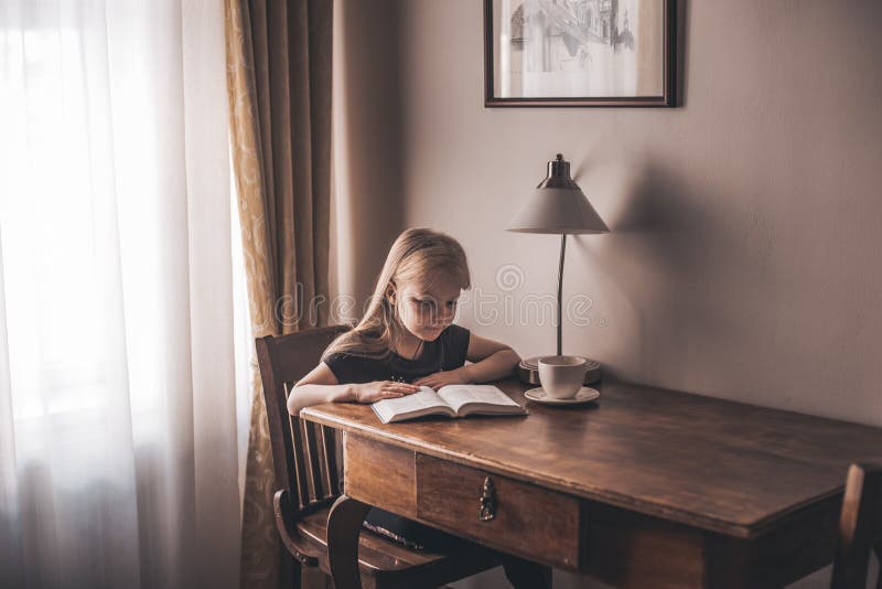 A Girl Sits at a Table Reading a Book Stock Photo - Image of learning ...